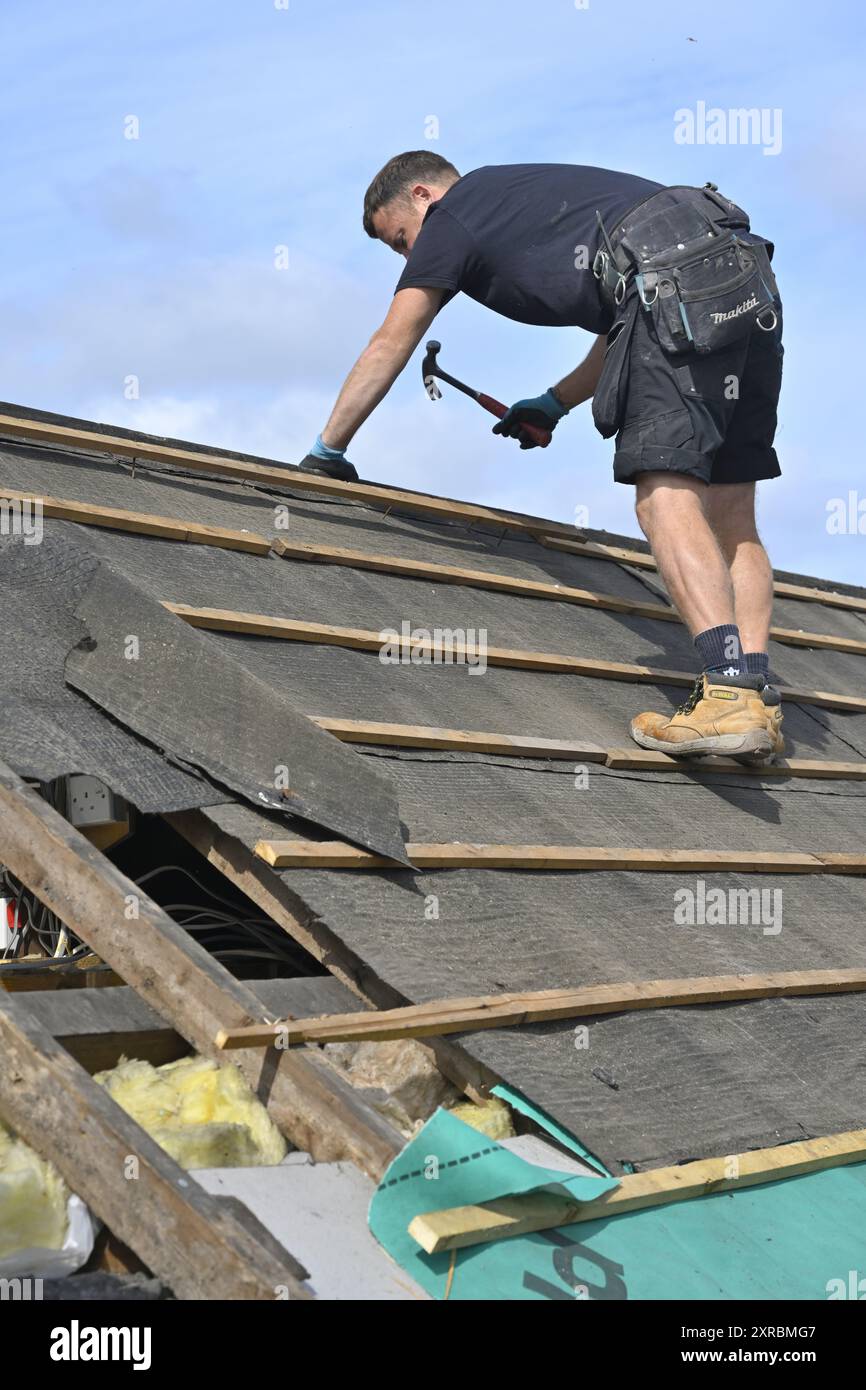 Roofing work, man on rooftop removing old felt nails with hammer to ...
