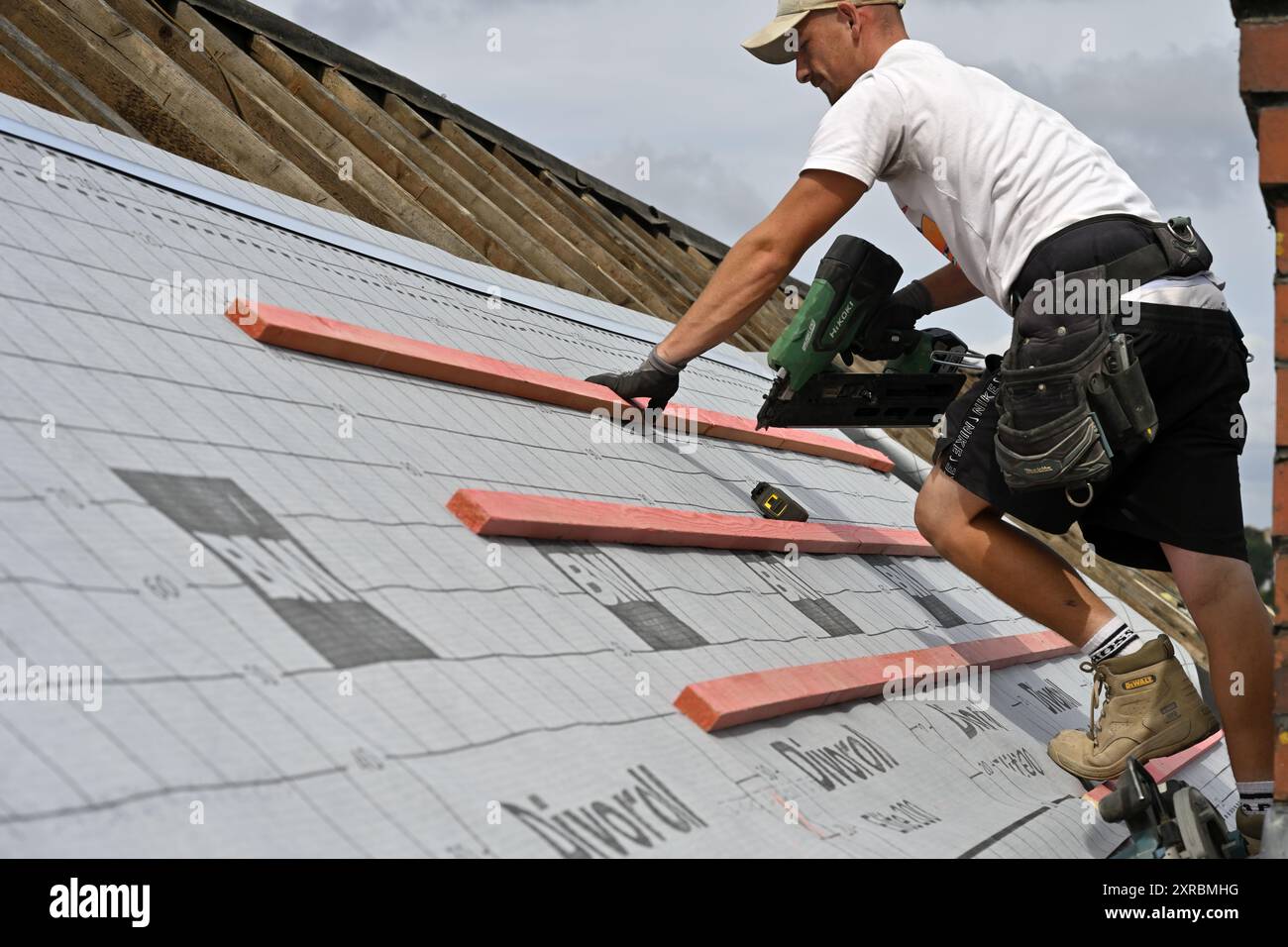 Roofing work, man using nail gun to fix new wooden battens on roofing ...