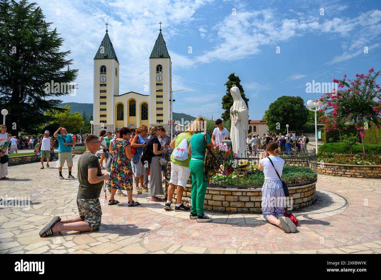 People praying around the statue of the Queen of Peace near the St ...