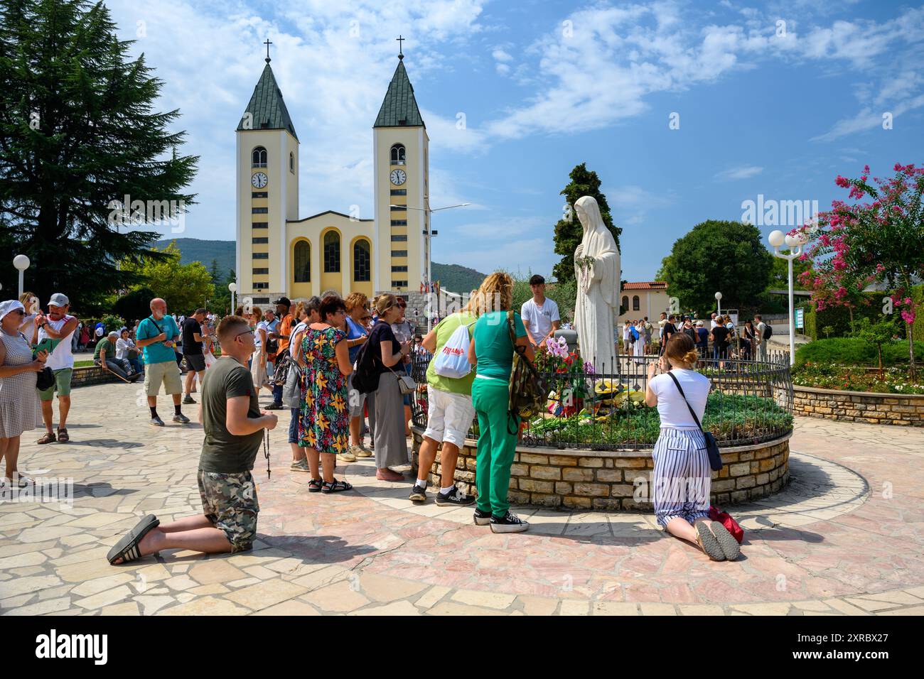 People praying around the statue of the Queen of Peace near the St ...
