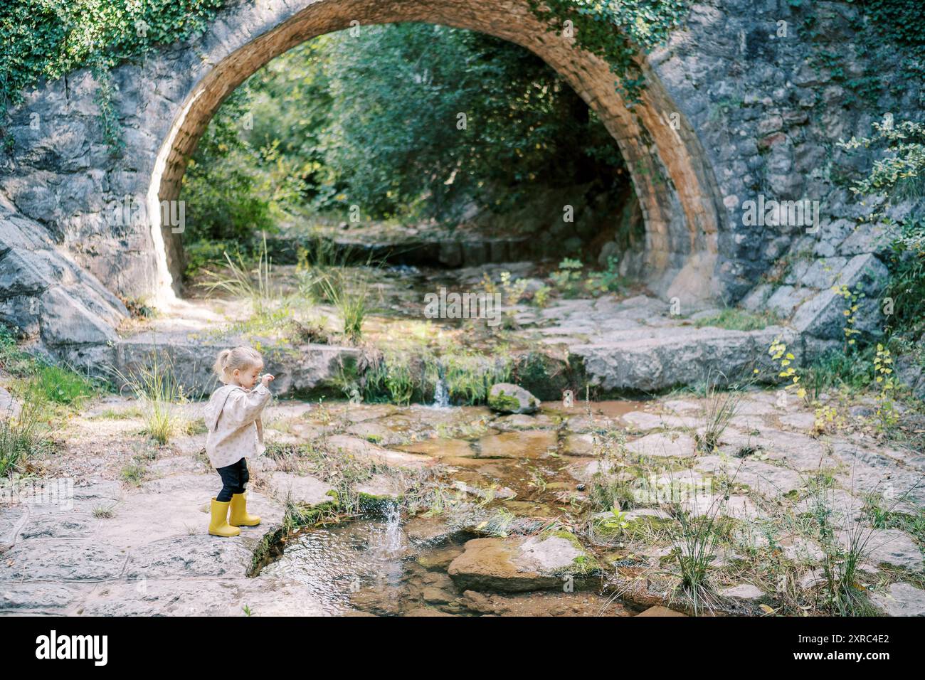 Little girl throws pebbles into the lake while standing on a paved bank ...