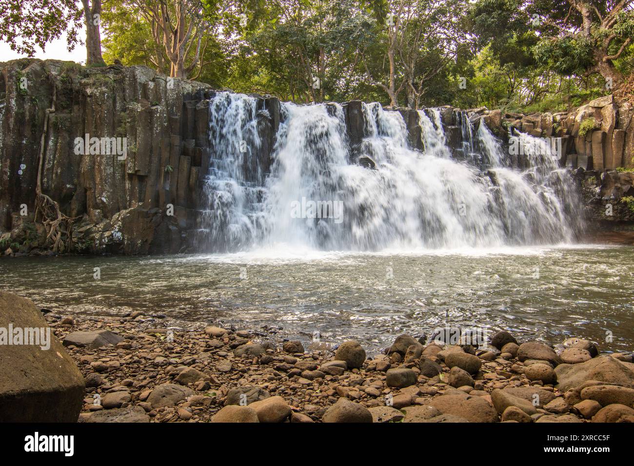 10 m high waterfall cascading over basal pillars into a basin, tropical ...
