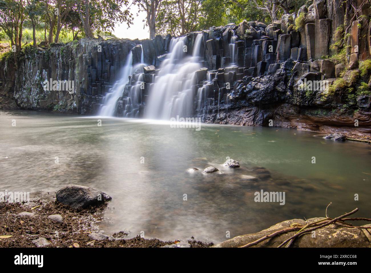 10 m high waterfall cascading over basal pillars into a basin, tropical ...