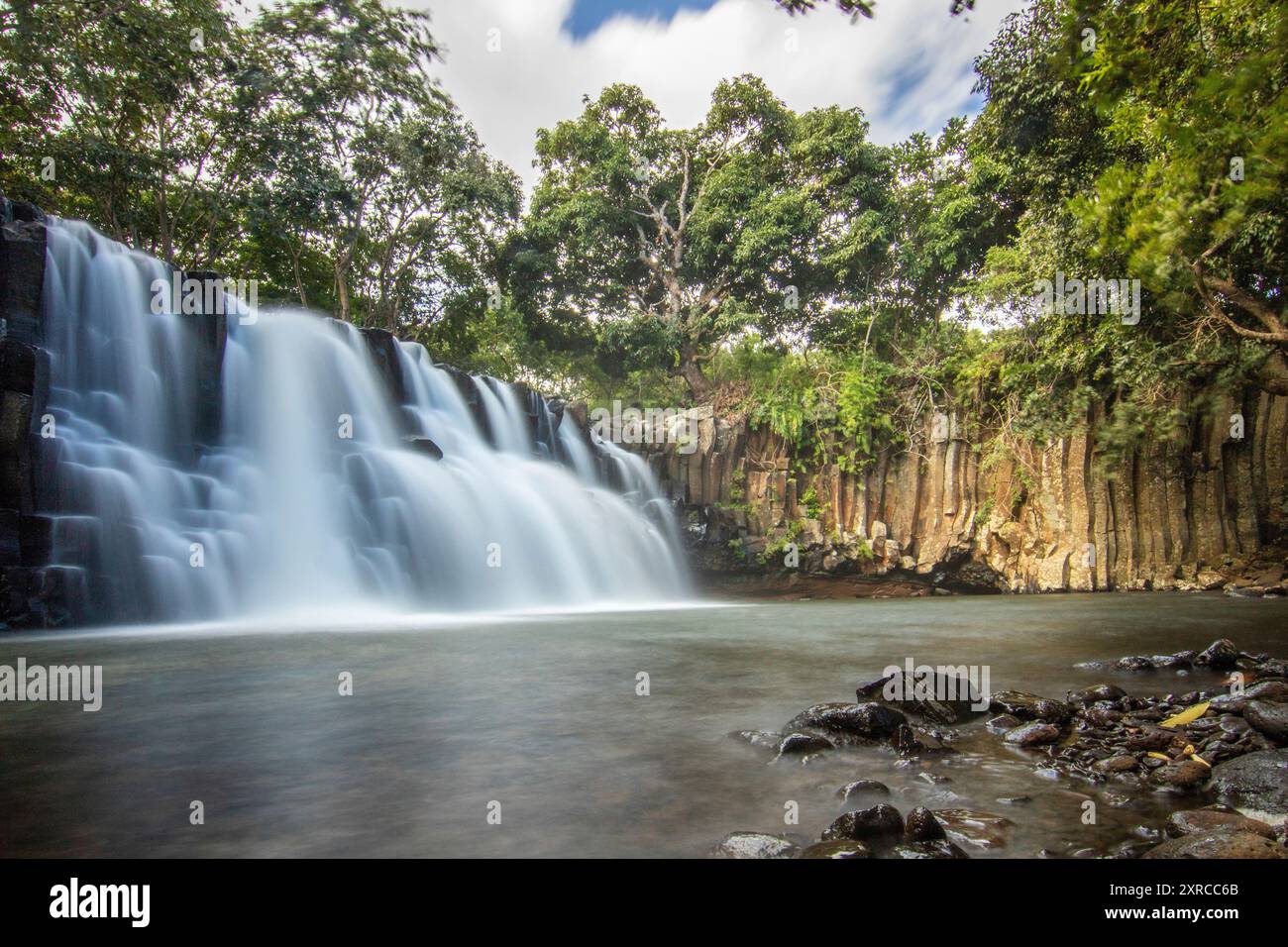 10 m high waterfall cascading over basal pillars into a basin, tropical ...