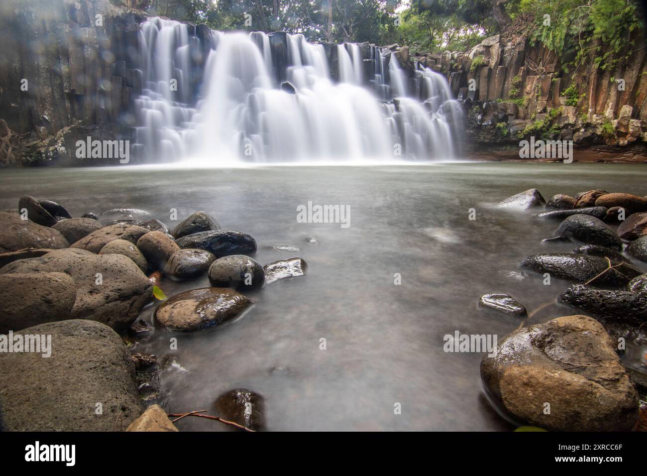 10 m high waterfall cascading over basal pillars into a basin, tropical ...
