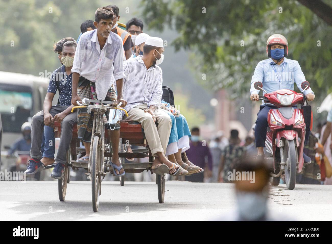 A rickshaw puller hauls morning commuters on the back of his flatbed ...
