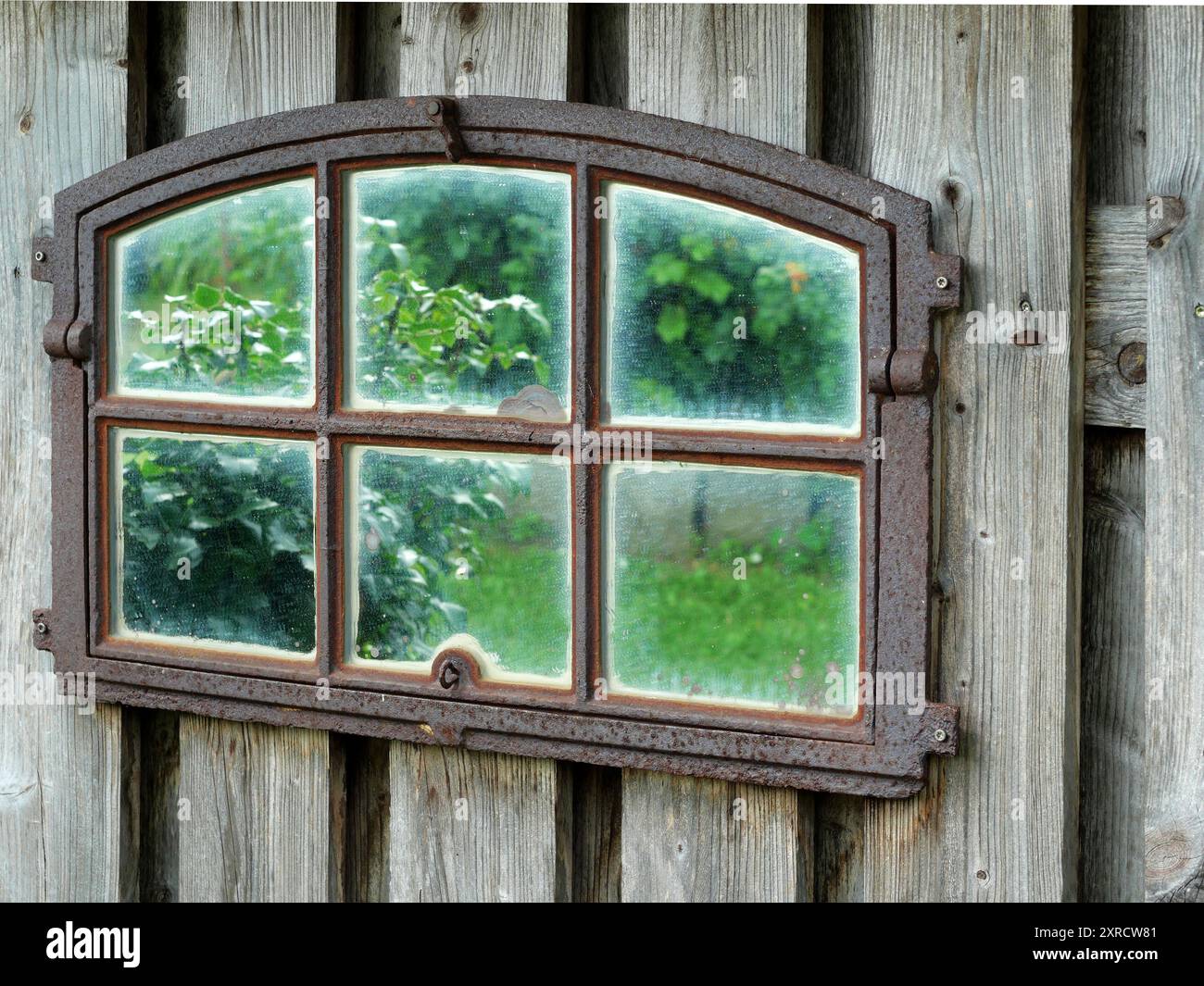 Rusty wrought iron window frame with mirror glass on a shed wall ...