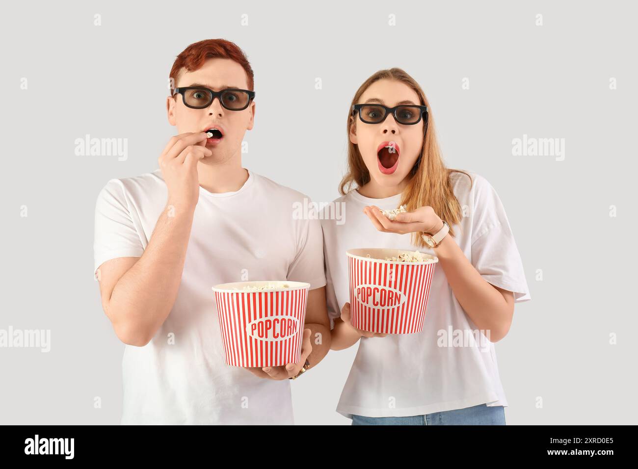 Shocked young couple in 3D glasses with popcorn on white background Stock Photo - Alamy