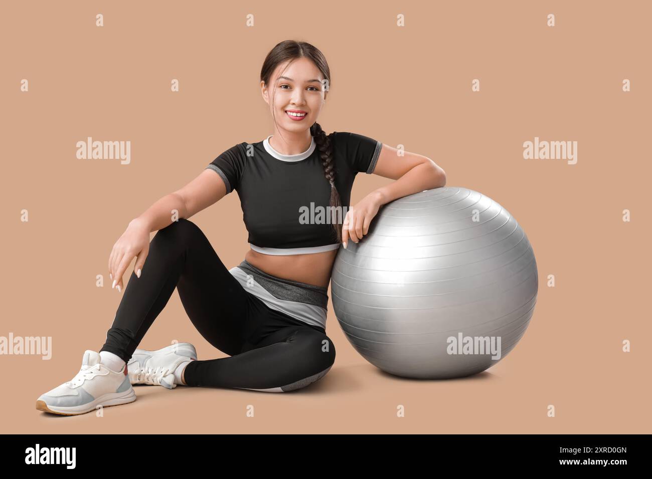 Sporty young Asian woman with fitball sitting on beige background Stock ...