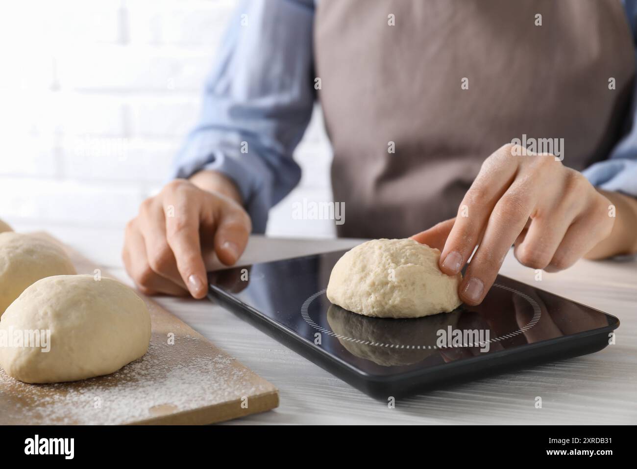 Woman weighing raw dough ball on kitchen scale at white wooden table ...