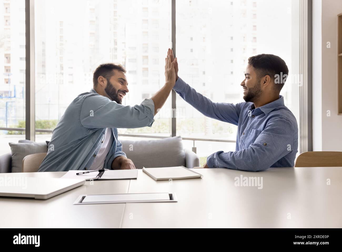 Two male business friends giving high five at office table Stock Photo ...