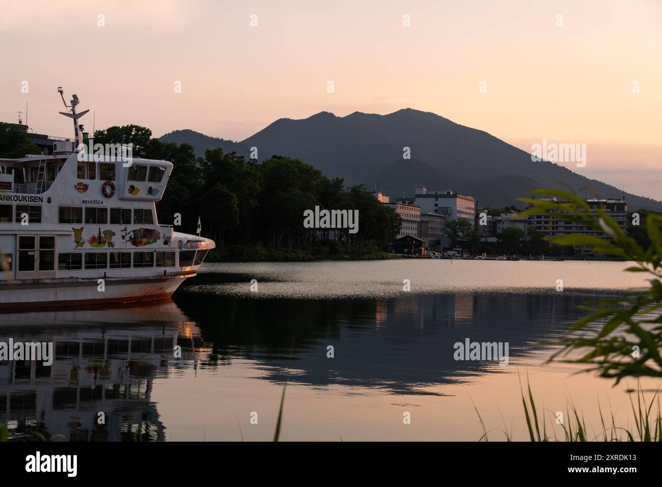 Lake Akan, Japan - July 23 2024: The sun sets over a cruise ship on the ...