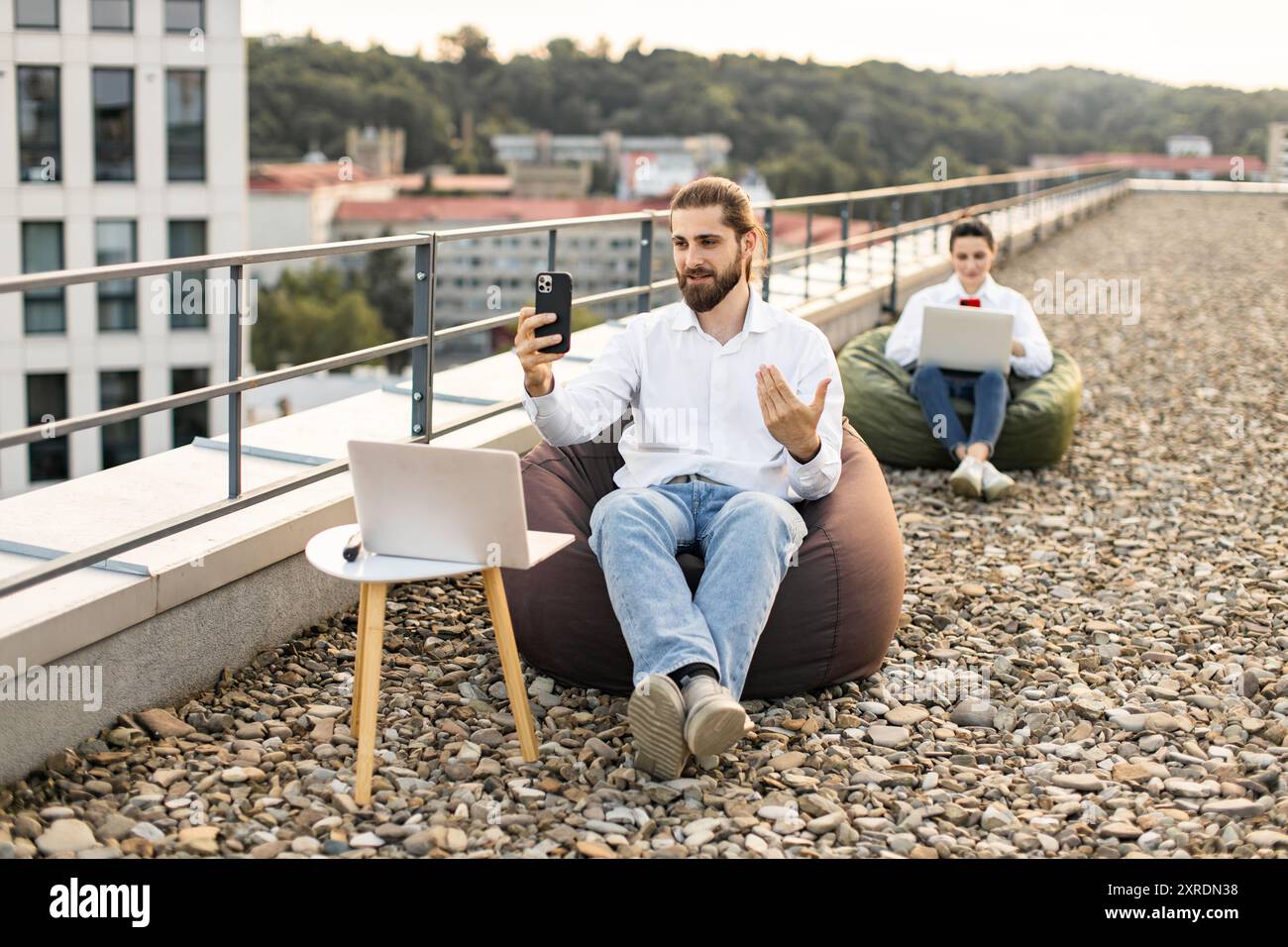 Businessmen working remotely on rooftop with laptops and smartphones ...