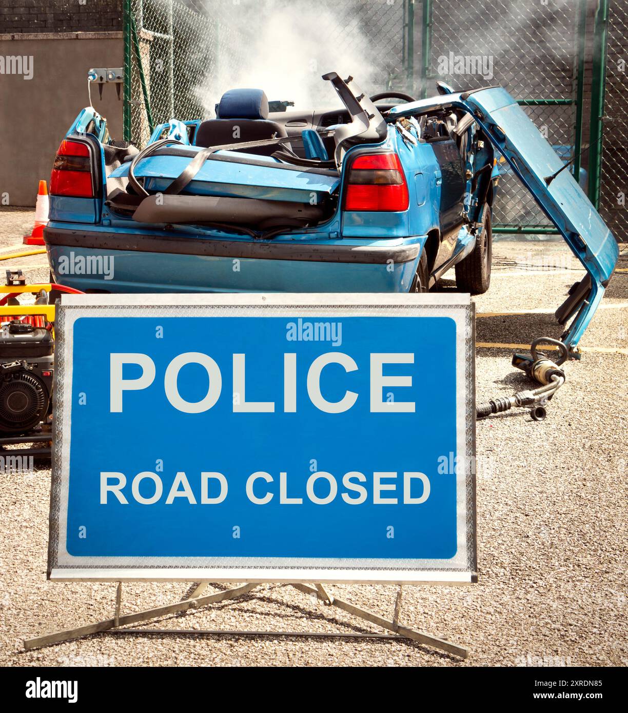 Incident sign ‘POLICE – ROAD CLOSED’ in front of smoking car wreckage ...