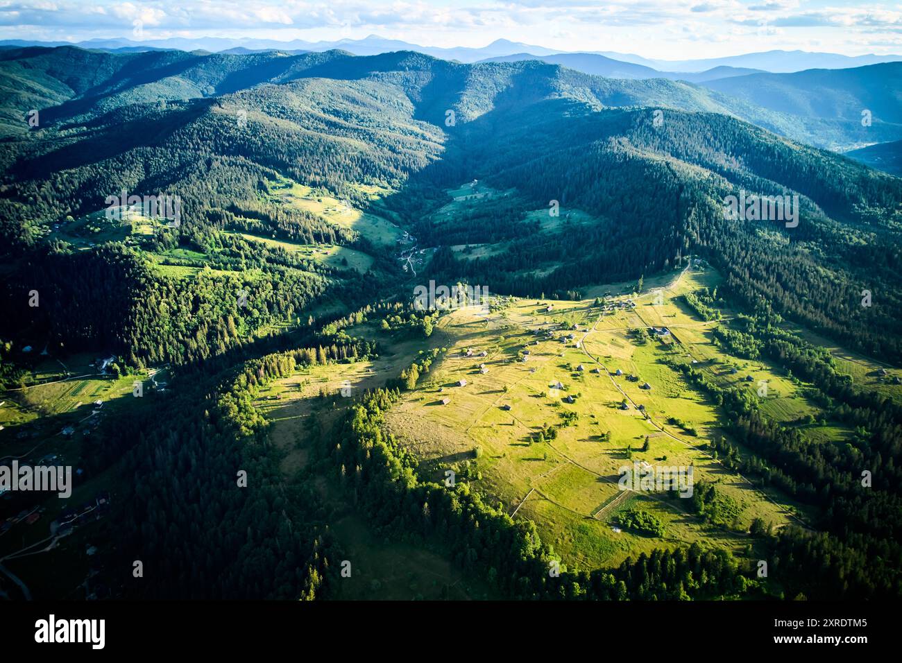 Aerial view of sunlit valley, dotted with small houses and winding ...