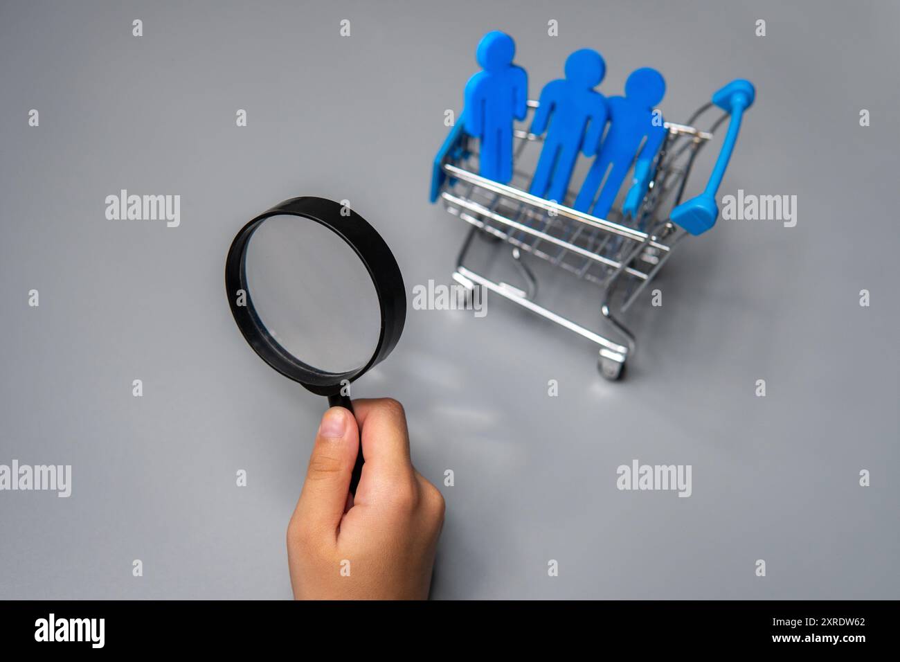 A hand holding a magnifying glass and miniature shopping cart filled ...