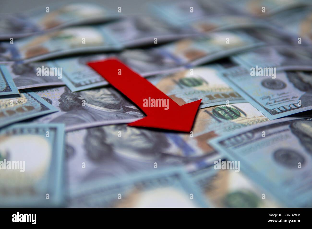 A red arrow pointing downwards on top of a pile of US dollar bills ...