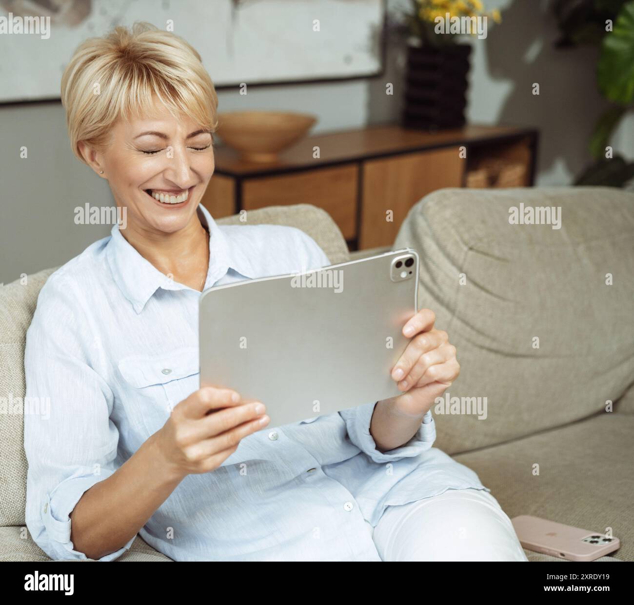 A woman smiles brightly as she interacts with her tablet, enjoying her ...