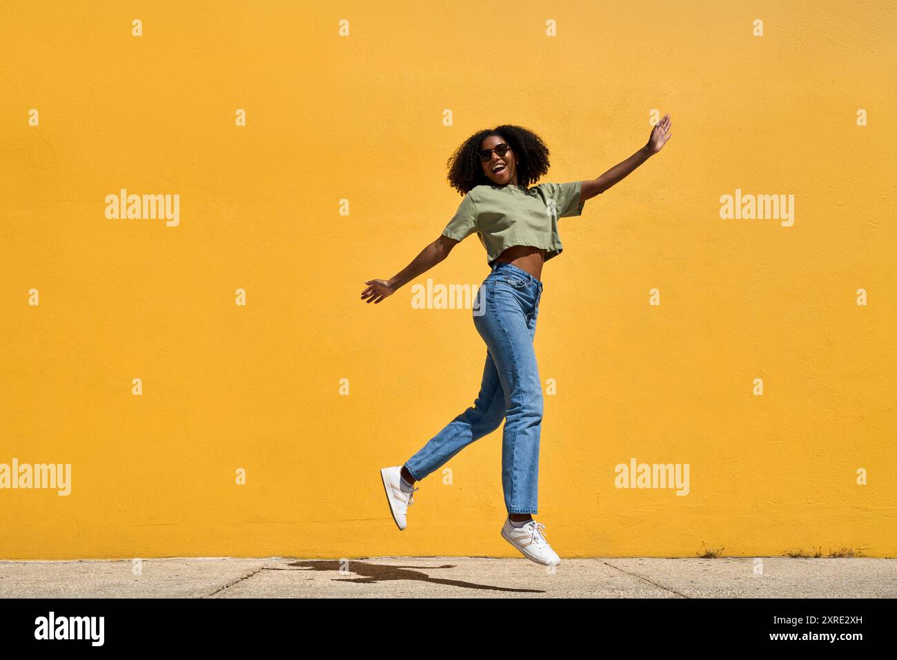 Happy funky young African American woman winner jumping at yellow wall ...