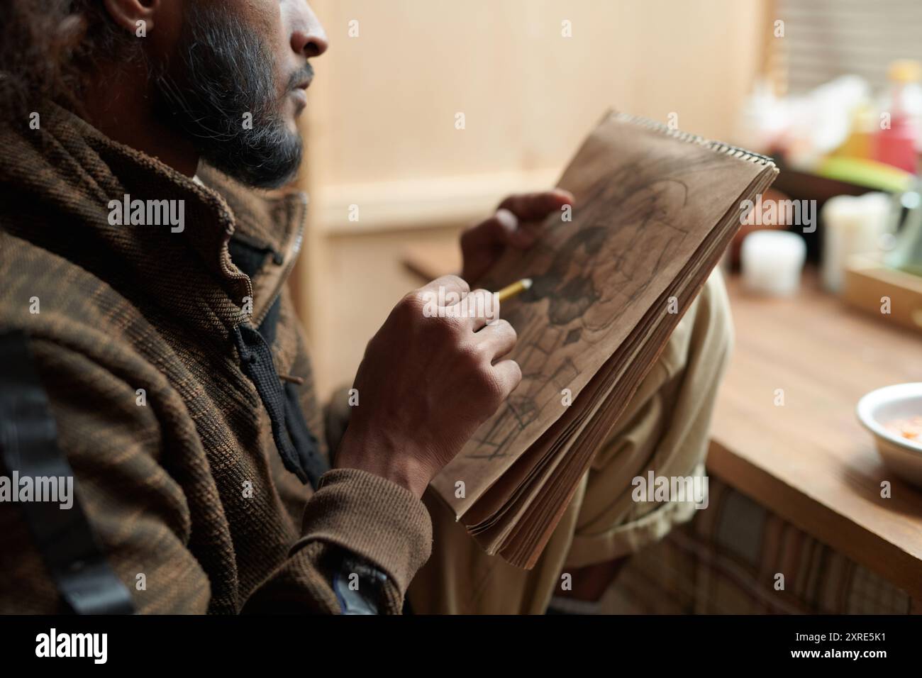 Man focusing on detailed sketching in spiral notebook while sitting in ...