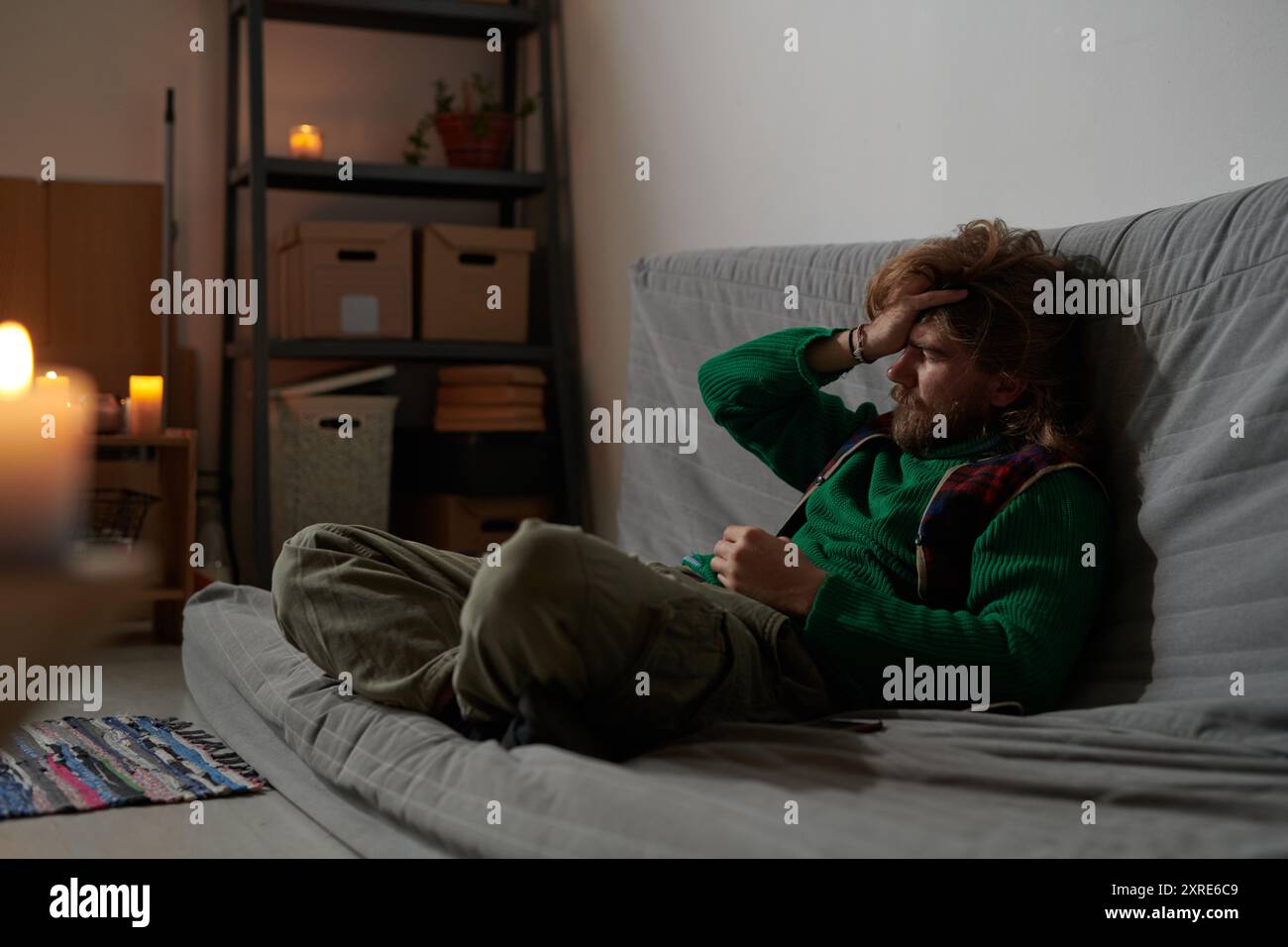 Man sitting on sofa in warm living room with dim light from candles ...