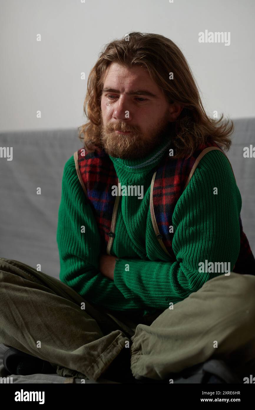 Man with shoulder-length hair and beard sitting cross-legged on a couch ...