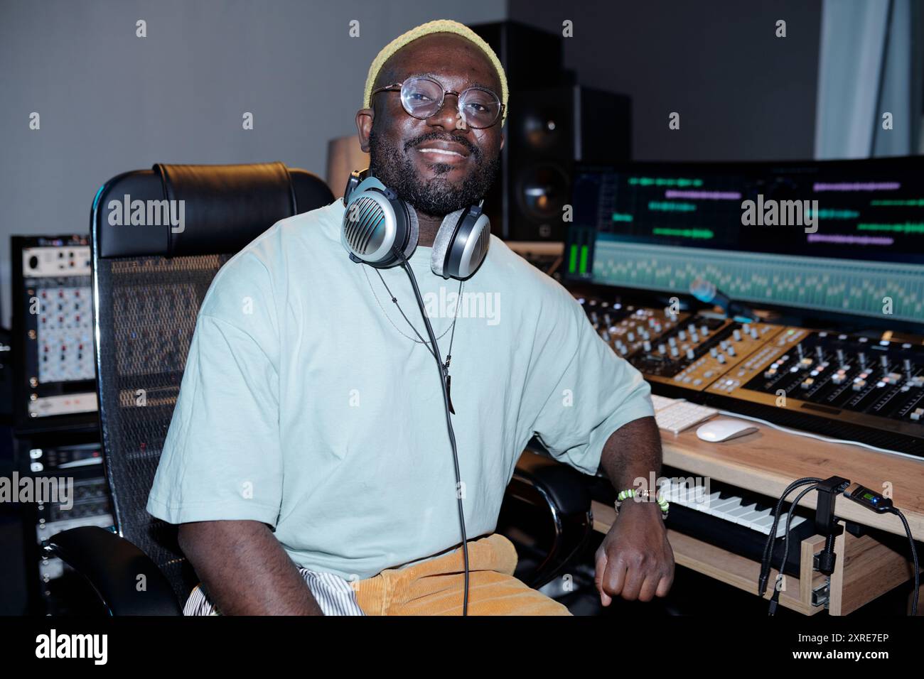 Man sitting in recording studio with headphones around neck, smiling ...