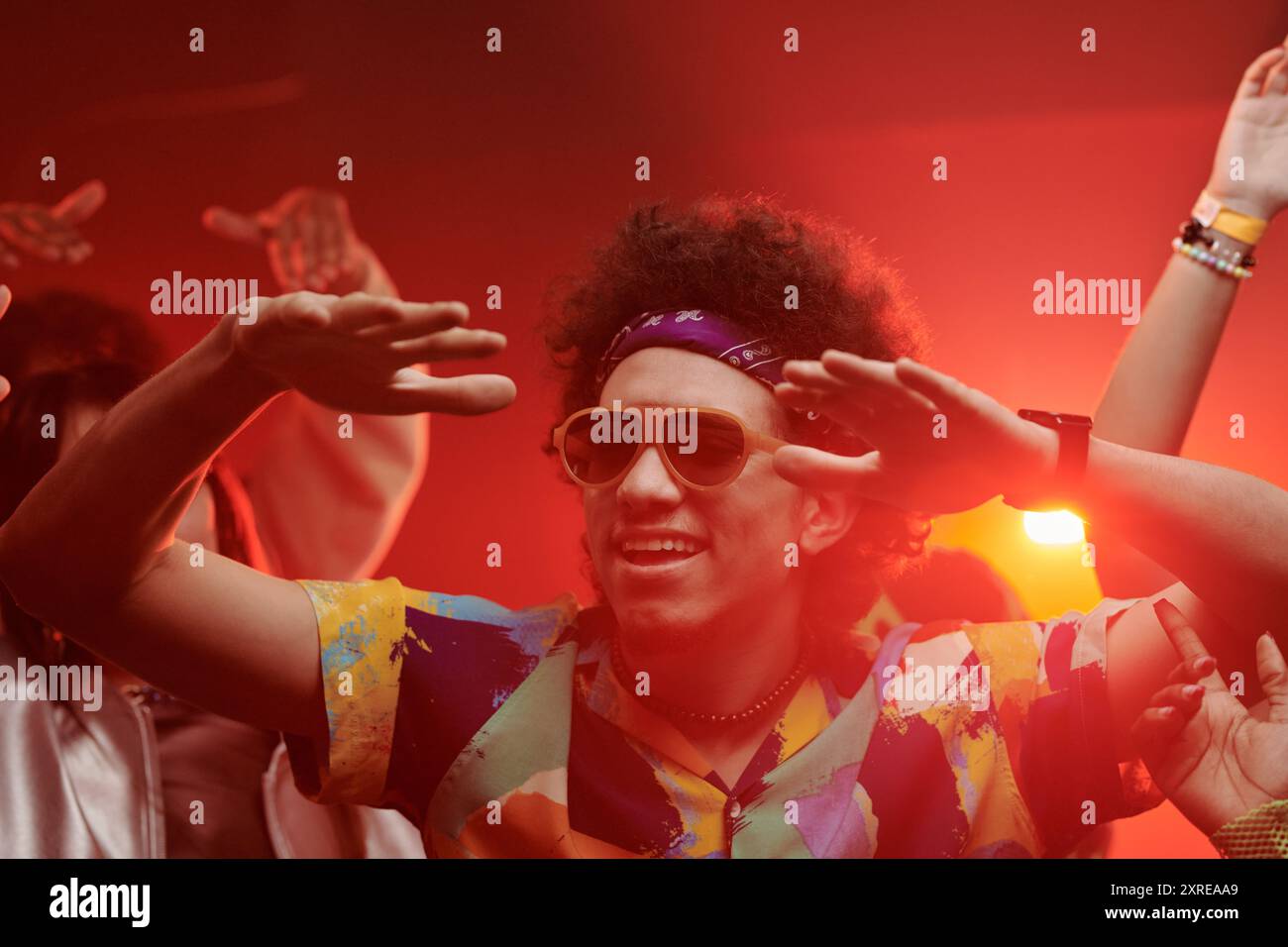 Happy young man in funky outfit keeping raised hands in front of his ...