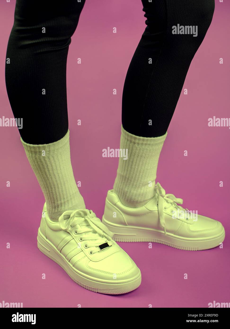 Close-up of female legs in white sneakers, back view, purple background ...