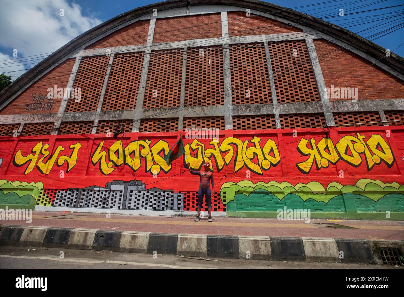 A man wearing a Spider-Man costume walks past a graffiti on a wall ...