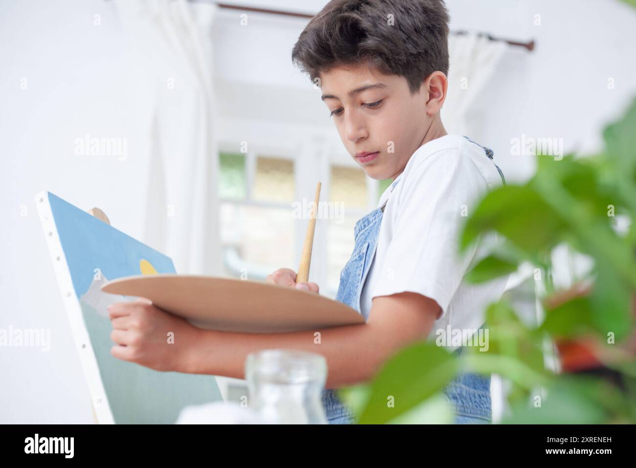A teenager concentrating on painting a landscape on a canvas at home ...