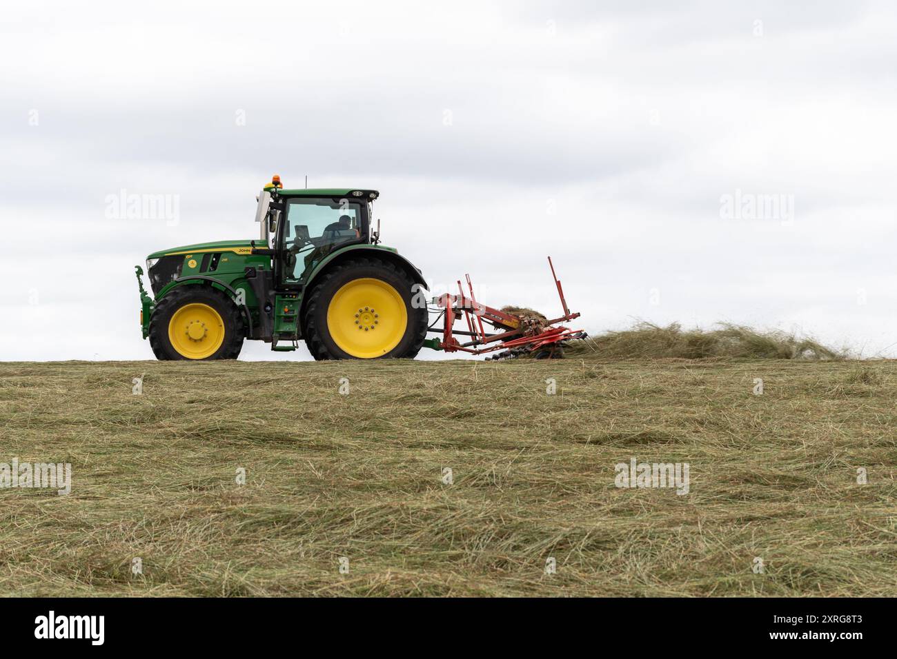 Farmer in tractor cutting grass in hay field or meadow to make feed for ...