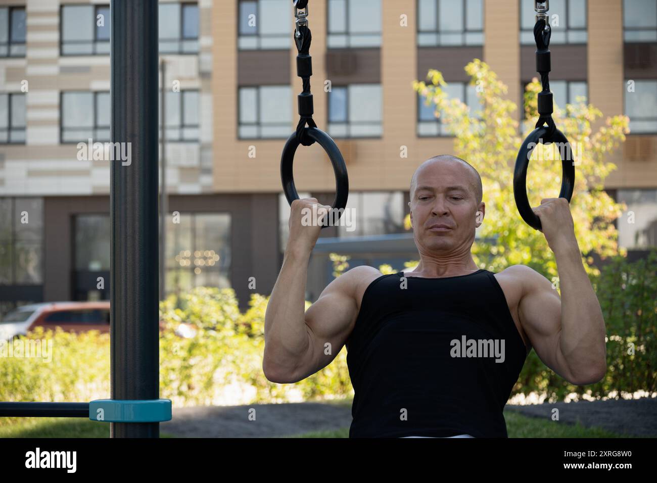 Athlete muscular fitness male pulling up on gymnastic rings at street ...