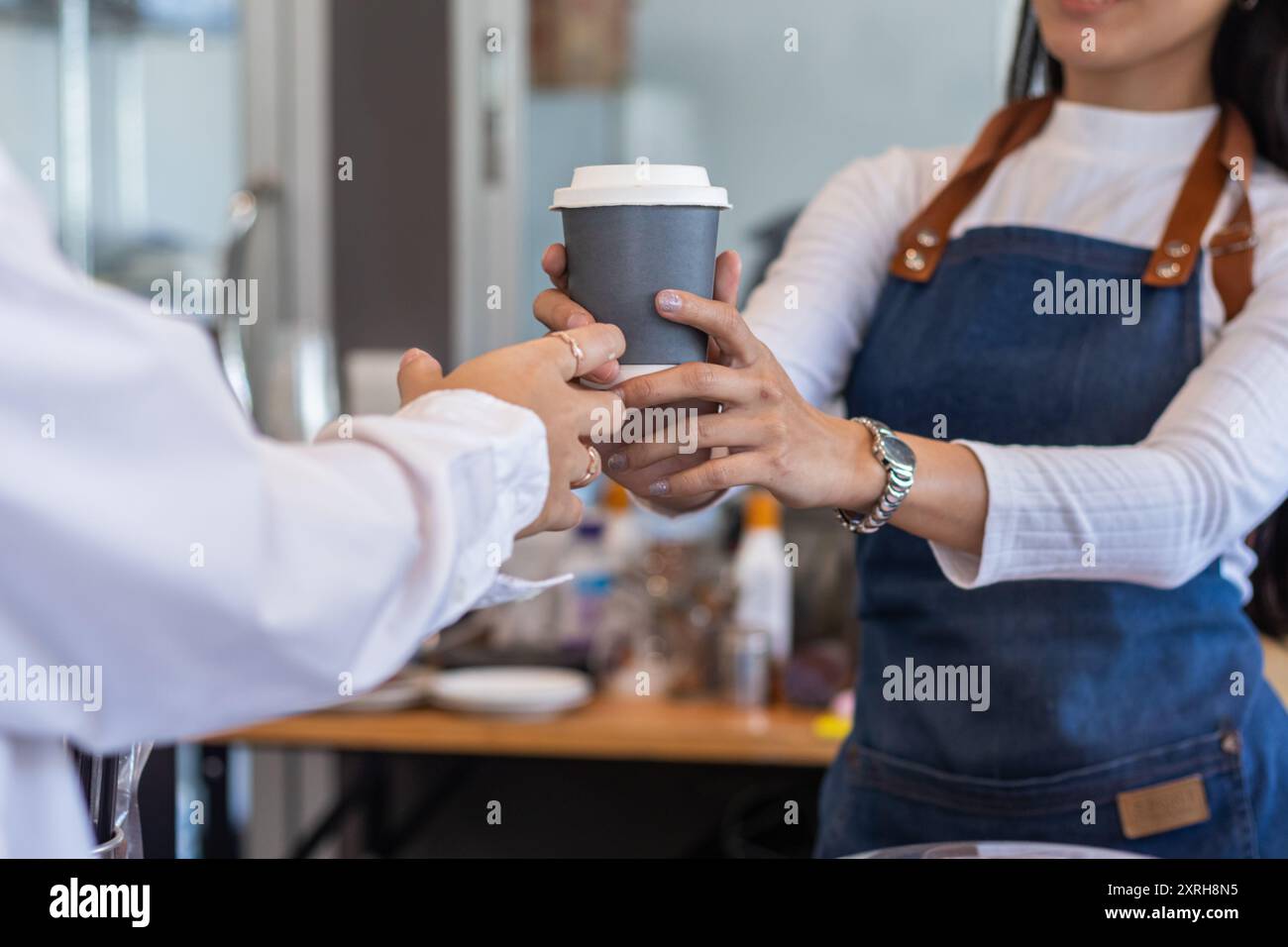 A beautiful Asian barista handing a cup of coffee to customers who wait ...