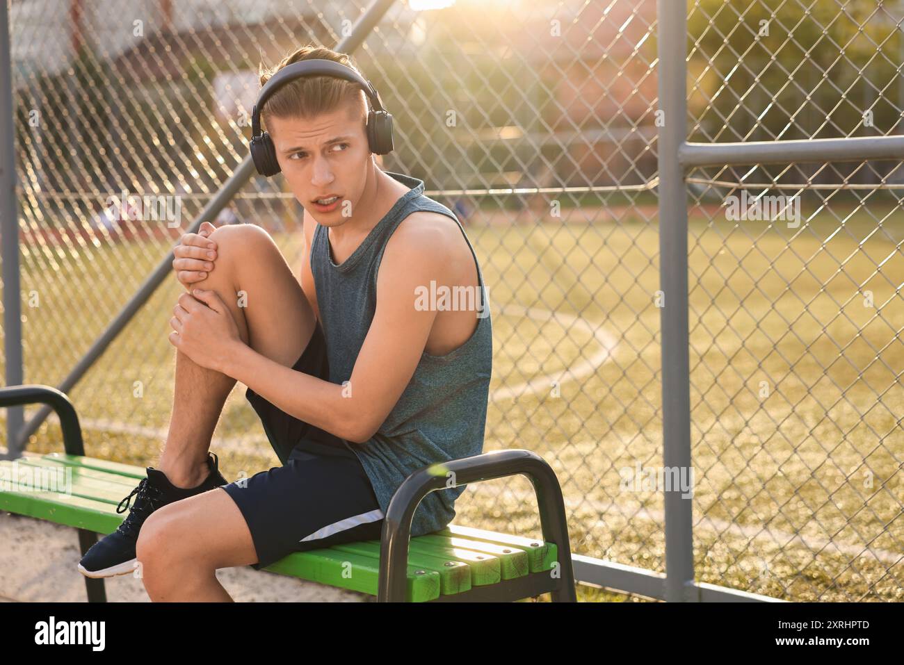 Sportsman with leg injury suffering from knee pain on bench at stadium ...