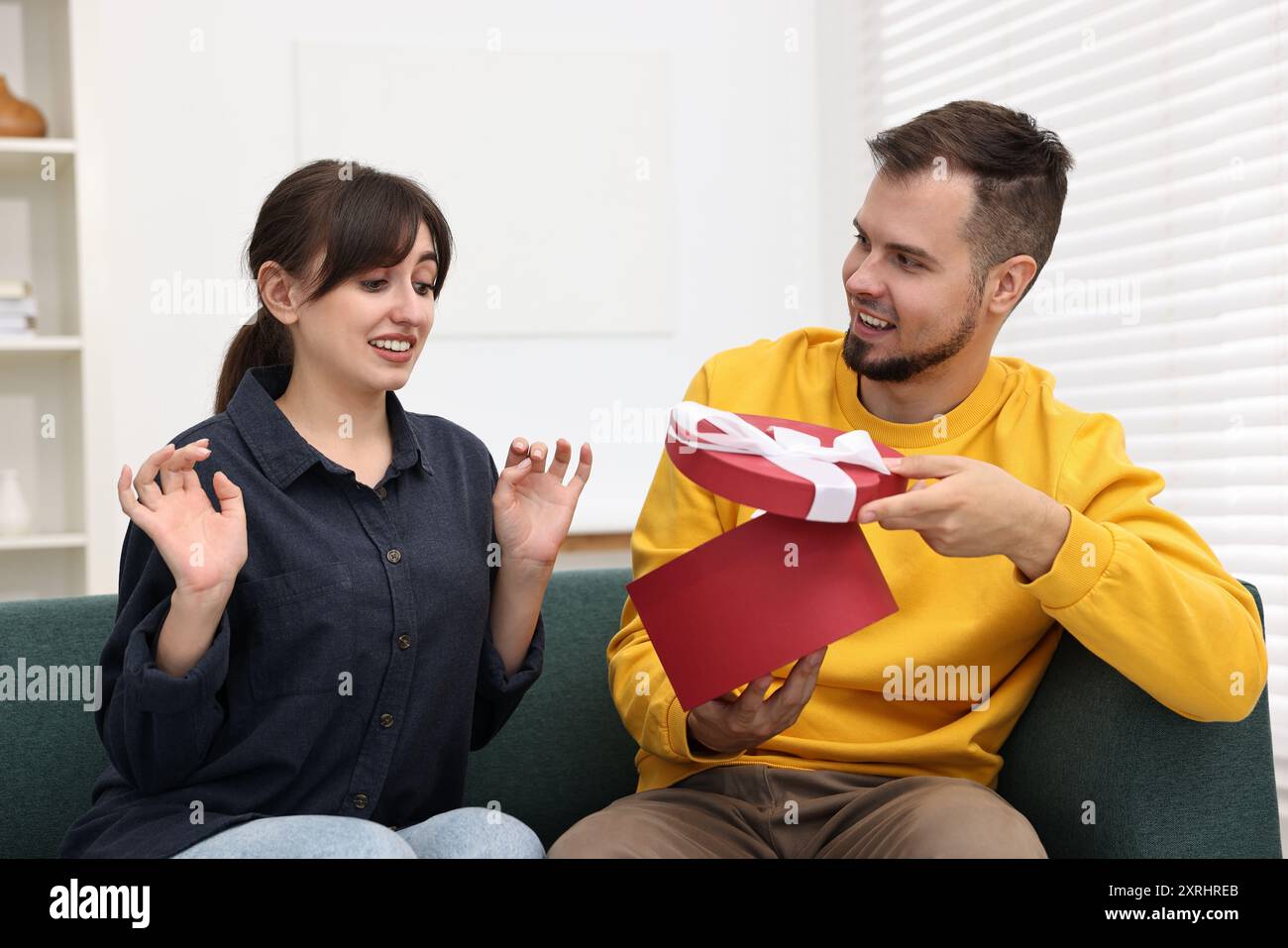 Smiling man presenting gift to embarrassed woman at home Stock Photo ...