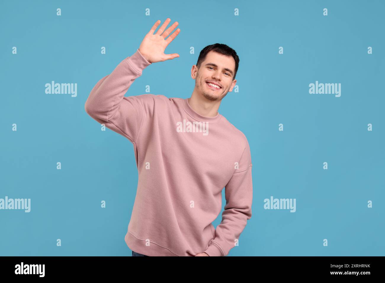 Happy young man waving on light blue background Stock Photo - Alamy