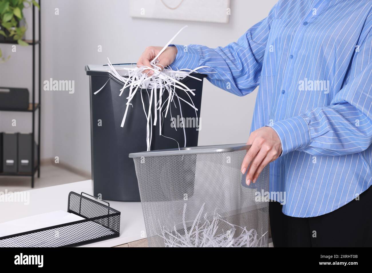 Woman putting shredded paper strips into trash bin at white table in ...