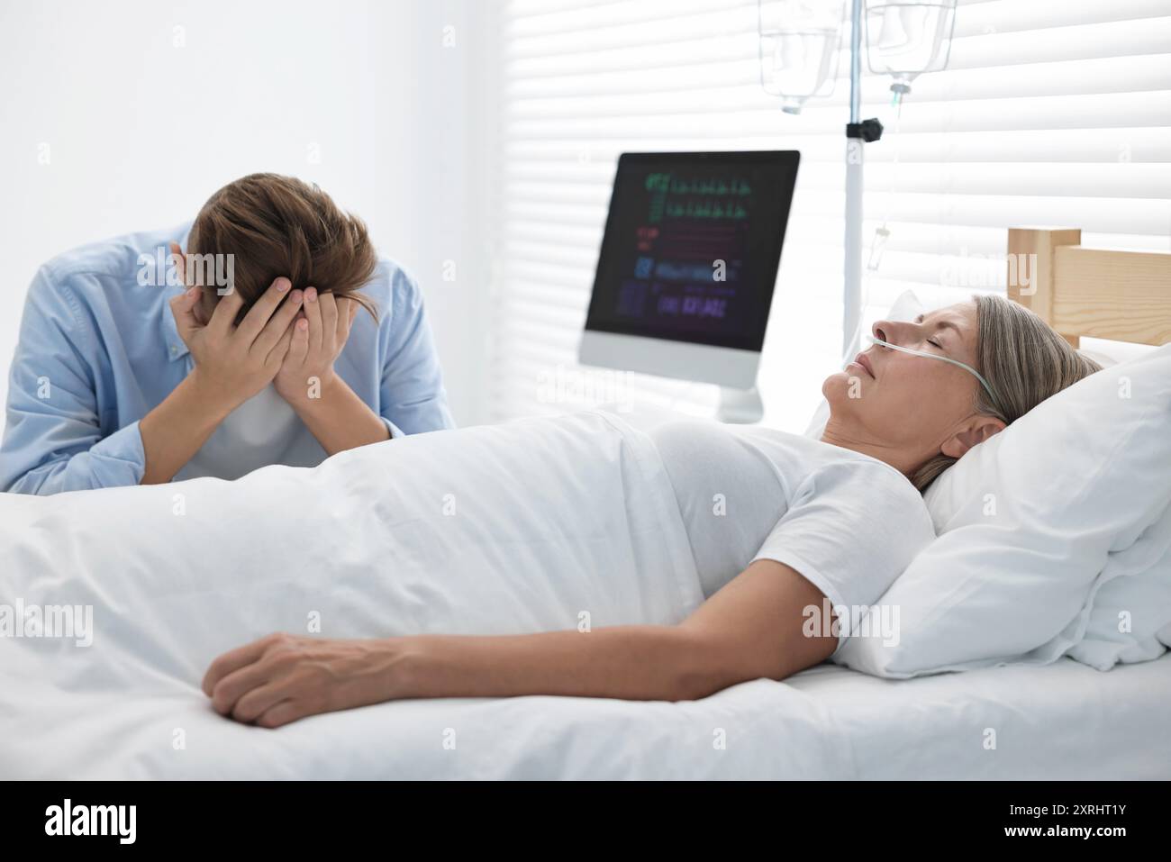 Coma patient. Sad young man near his unconscious mother in hospital ...