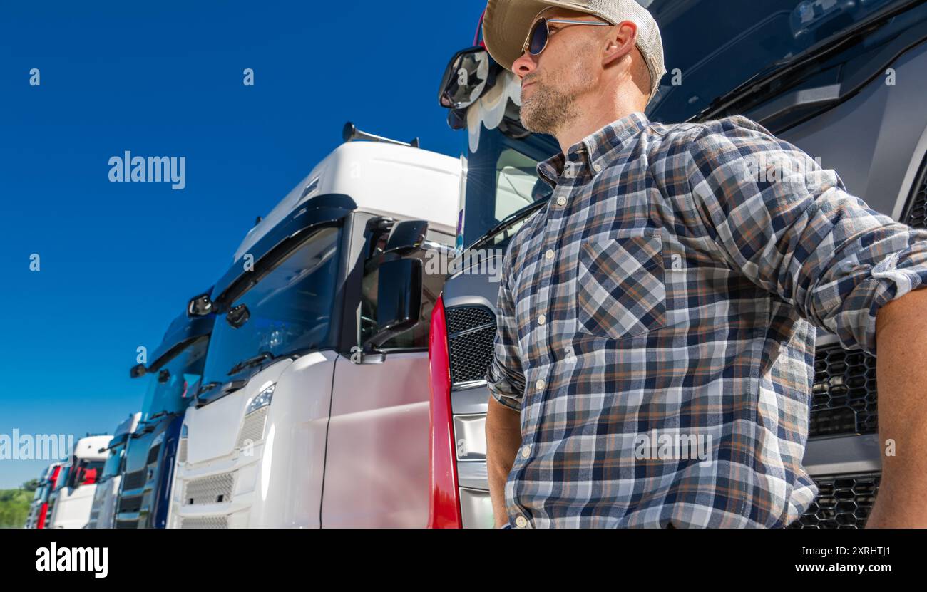 A truck driver poses next to a lineup of trucks, showcasing pride in ...