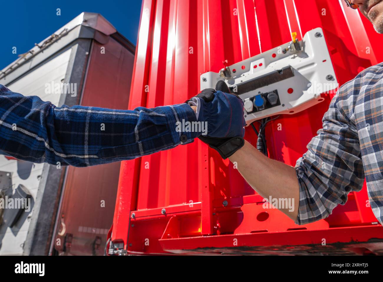Two workers shake hands in front of a red shipping container ...