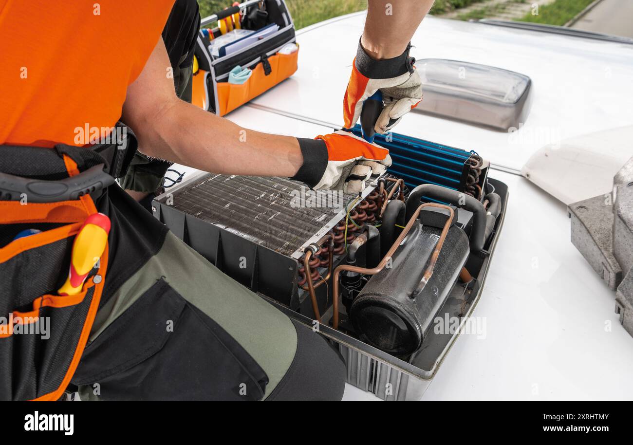 A technician adjusts components of a rooftop RV Camper HVAC unit, using tools from an open ...