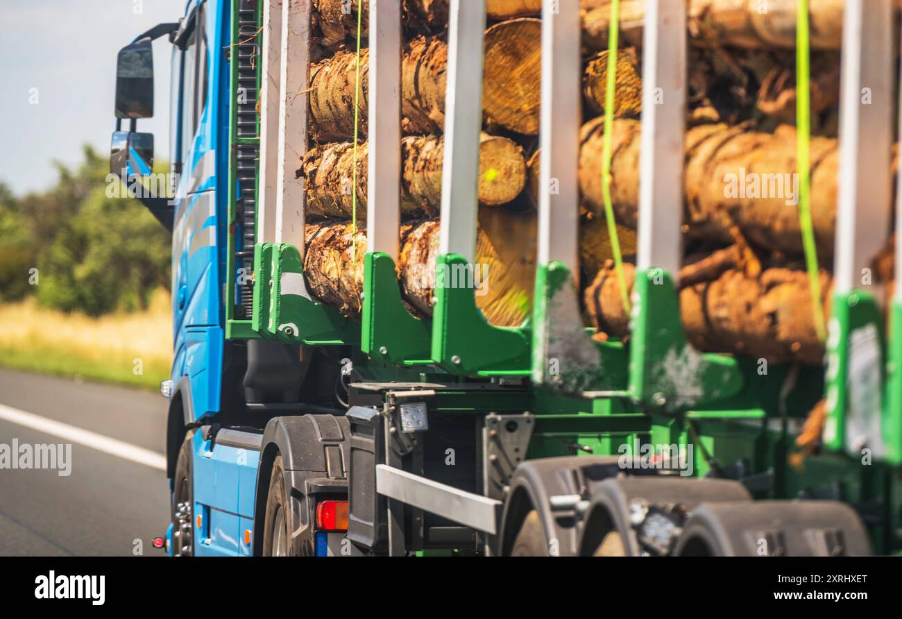 A blue truck loaded with logs drives on a rural highway under clear ...