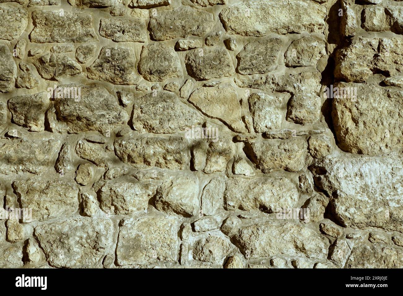 Textured boulders form an ancient stone wall with natural light creating shadow patterns Stock ...