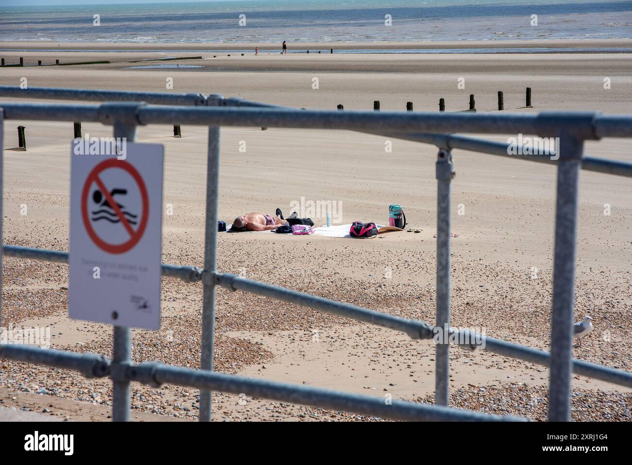 A man takes a sunbath on the beach at low tide as 'Swimming not advised ...