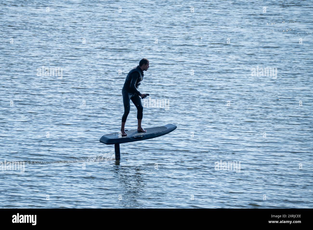 Surfer glides above calm water on electric hydrofoil board ...