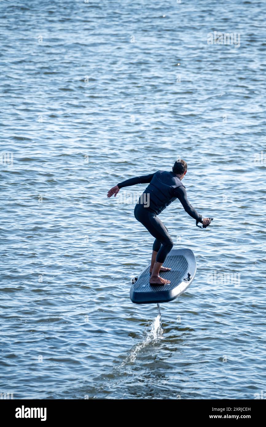 Surfer balances on electric hydrofoil board, gliding above rippling ...