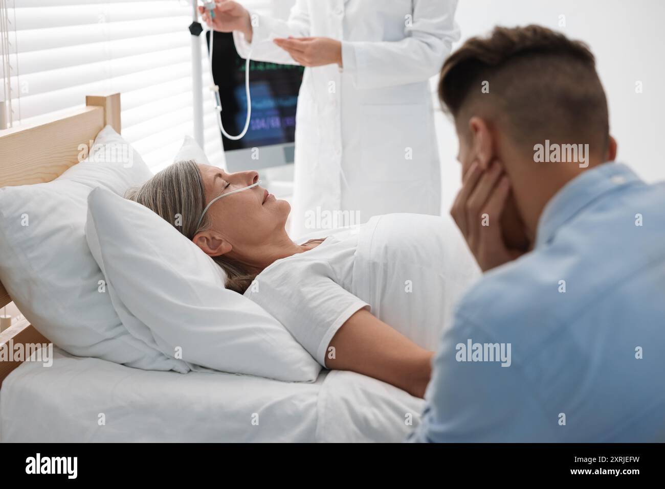 Coma patient. Sad young man near his unconscious mother in hospital ...