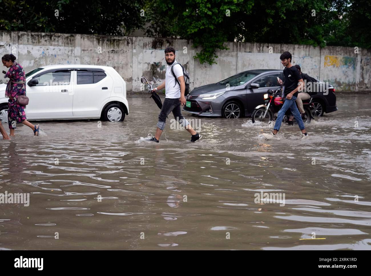 People walk through a flooded road caused by heavy monsoon rainfall in Lahore, Pakistan, Sunday ...