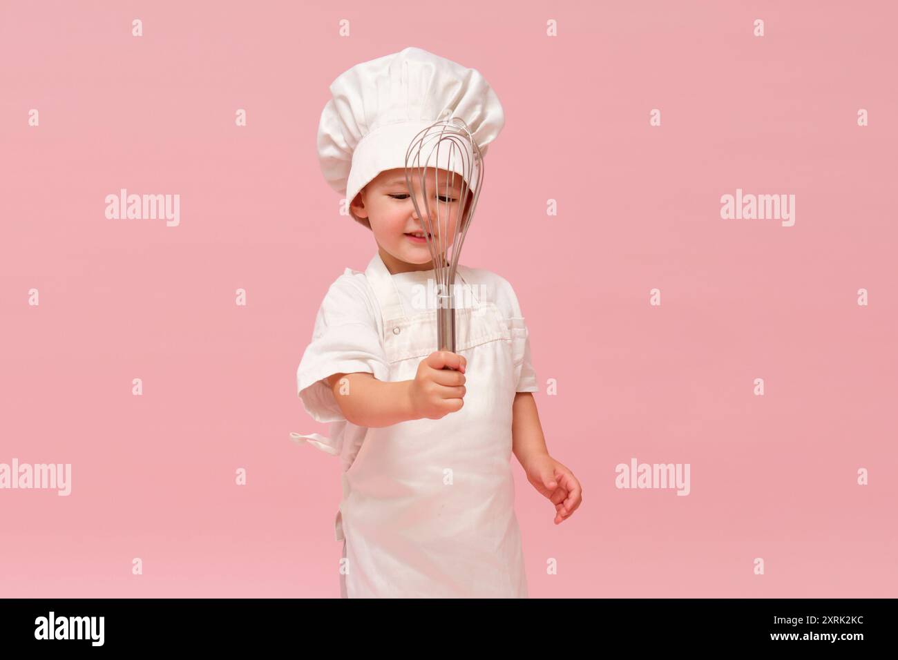 A young child wearing a chef's hat and apron holding a whisk. Studio ...